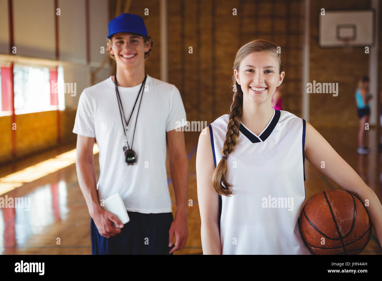Portrait of smiling basketball player with male coach standing in court ...