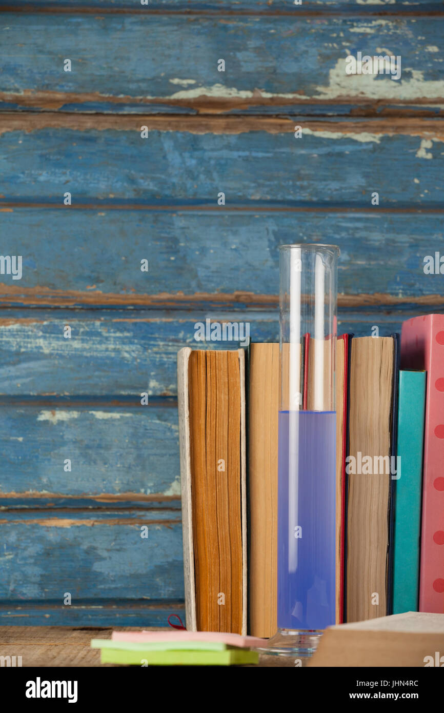 Stack of books, chemical test tube and sticky notes against blue wooden ...
