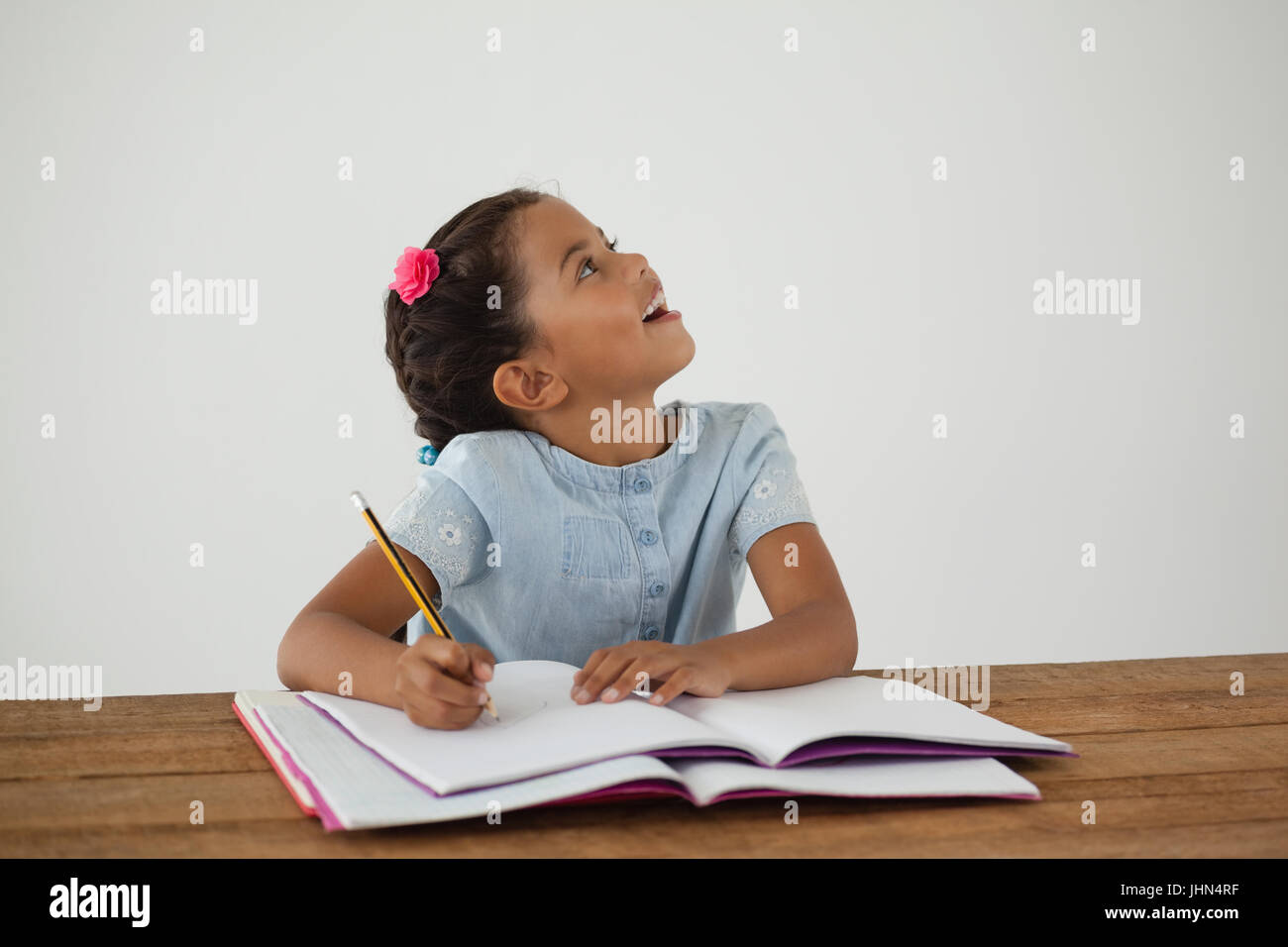 Portrait of young girl writing in her book against white background ...