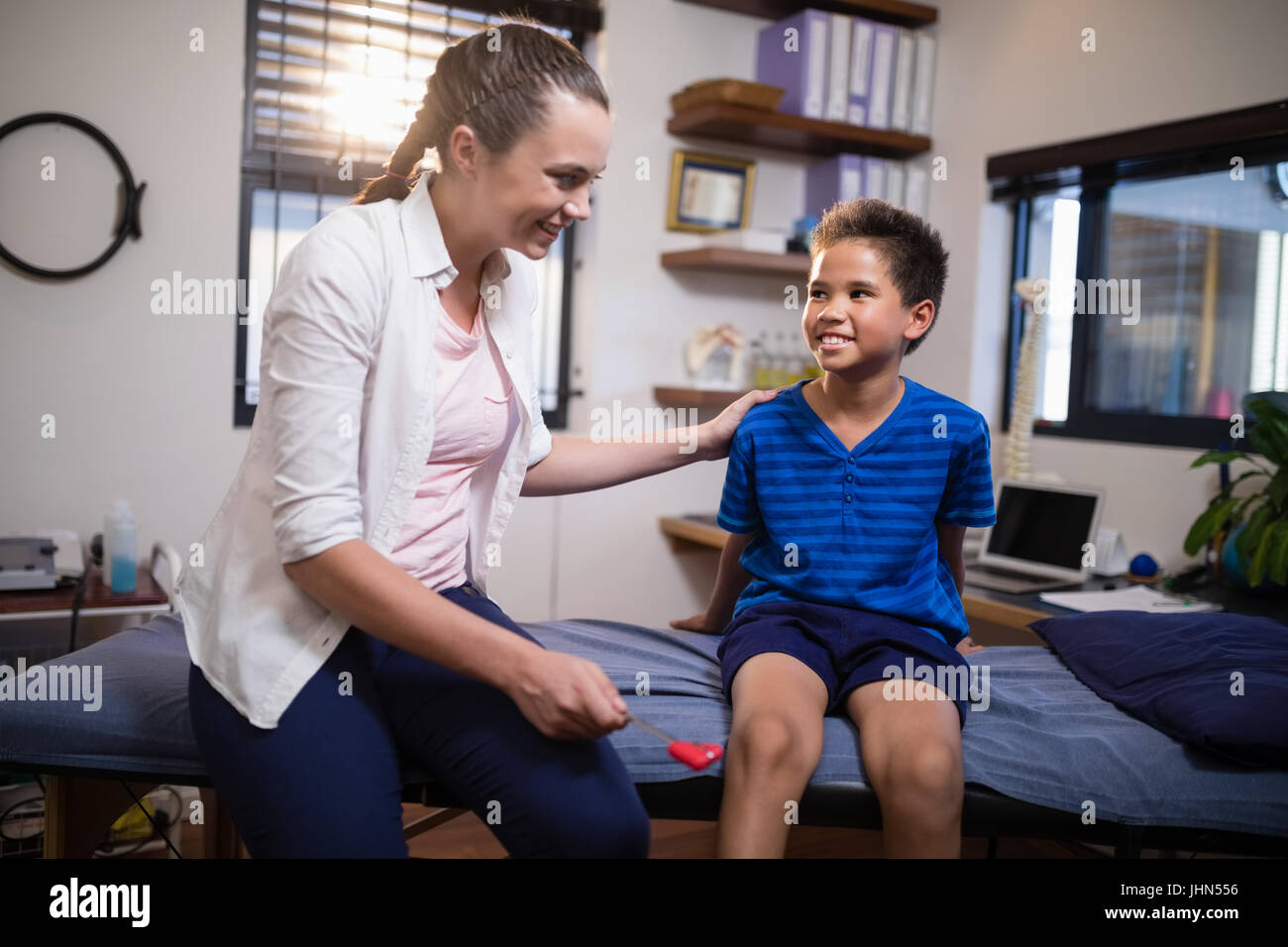 Smiling female therapist looking at boy while hitting at knee with ...