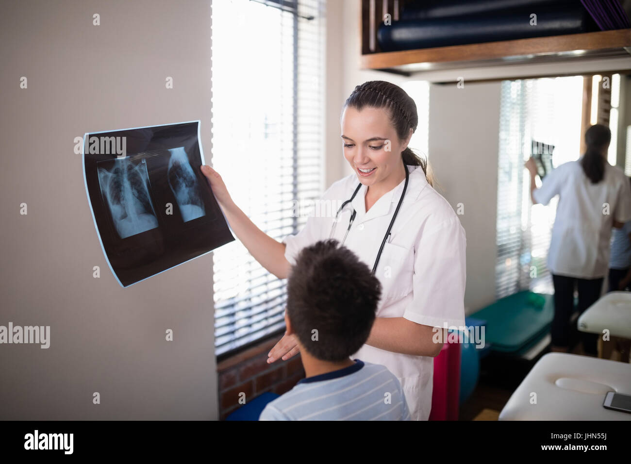 Female therapist holding x-ray while looking at boy in hospital ward ...