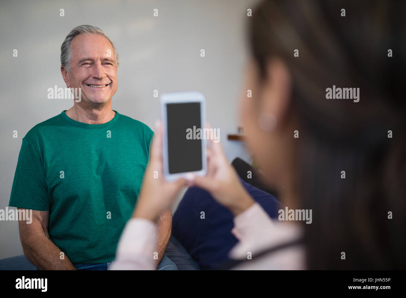 Female therapist photographing senior male patient from mobile phone at ...