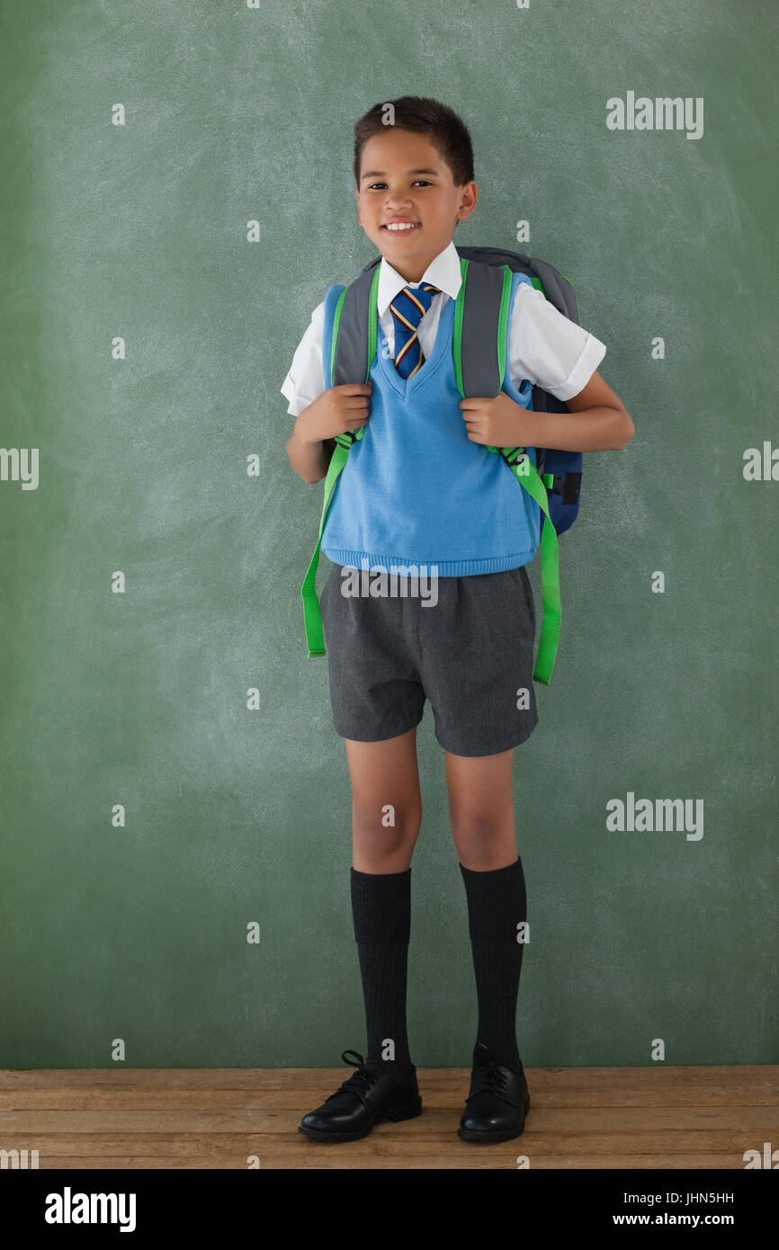 Portrait of schoolboy standing in front of chalkboard in classroom at ...
