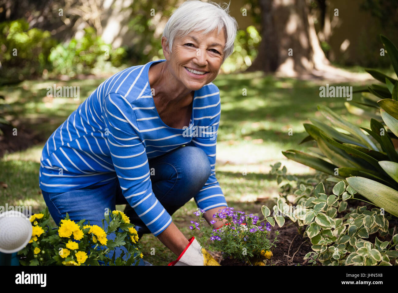 Portrait of happy senior woman kneeling while planting flowers in ...