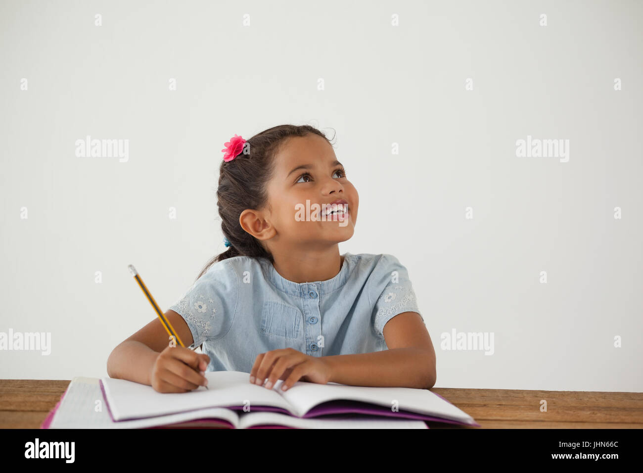 Portrait of young girl writing in her book against white background ...