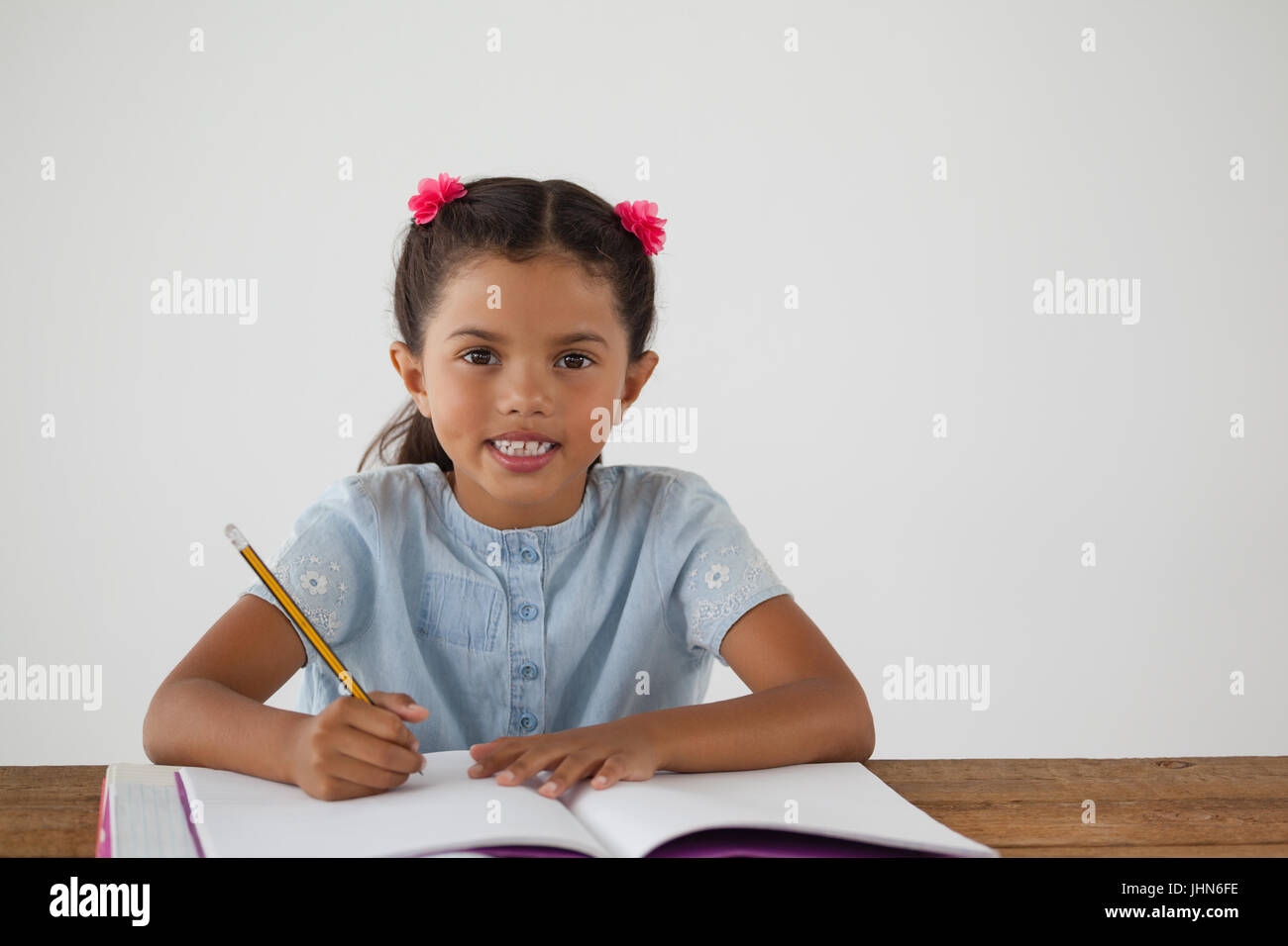 Portrait of young girl writing in her book against white background ...