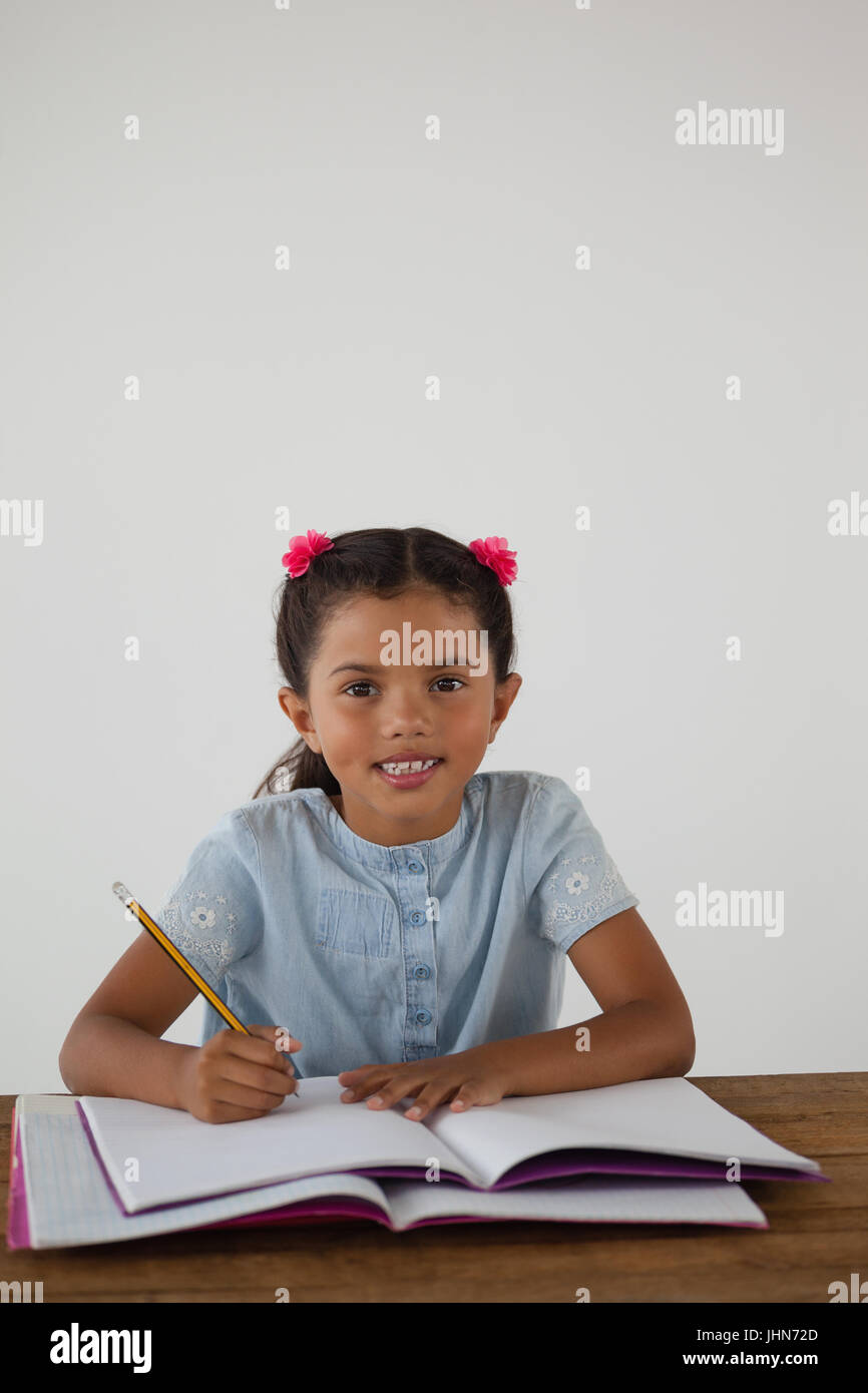 Portrait of young girl writing in her book against white background ...