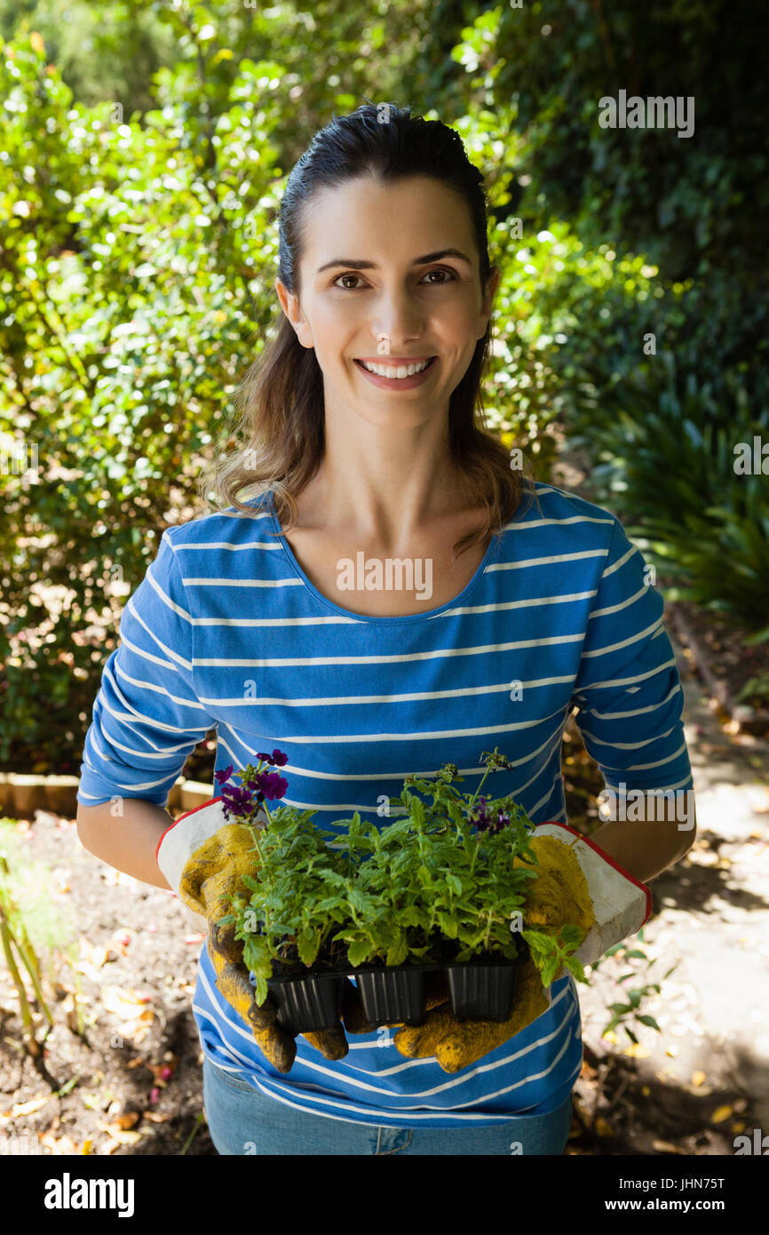 Portrait of smiling beautiful woman standing with seedlings at backyard ...