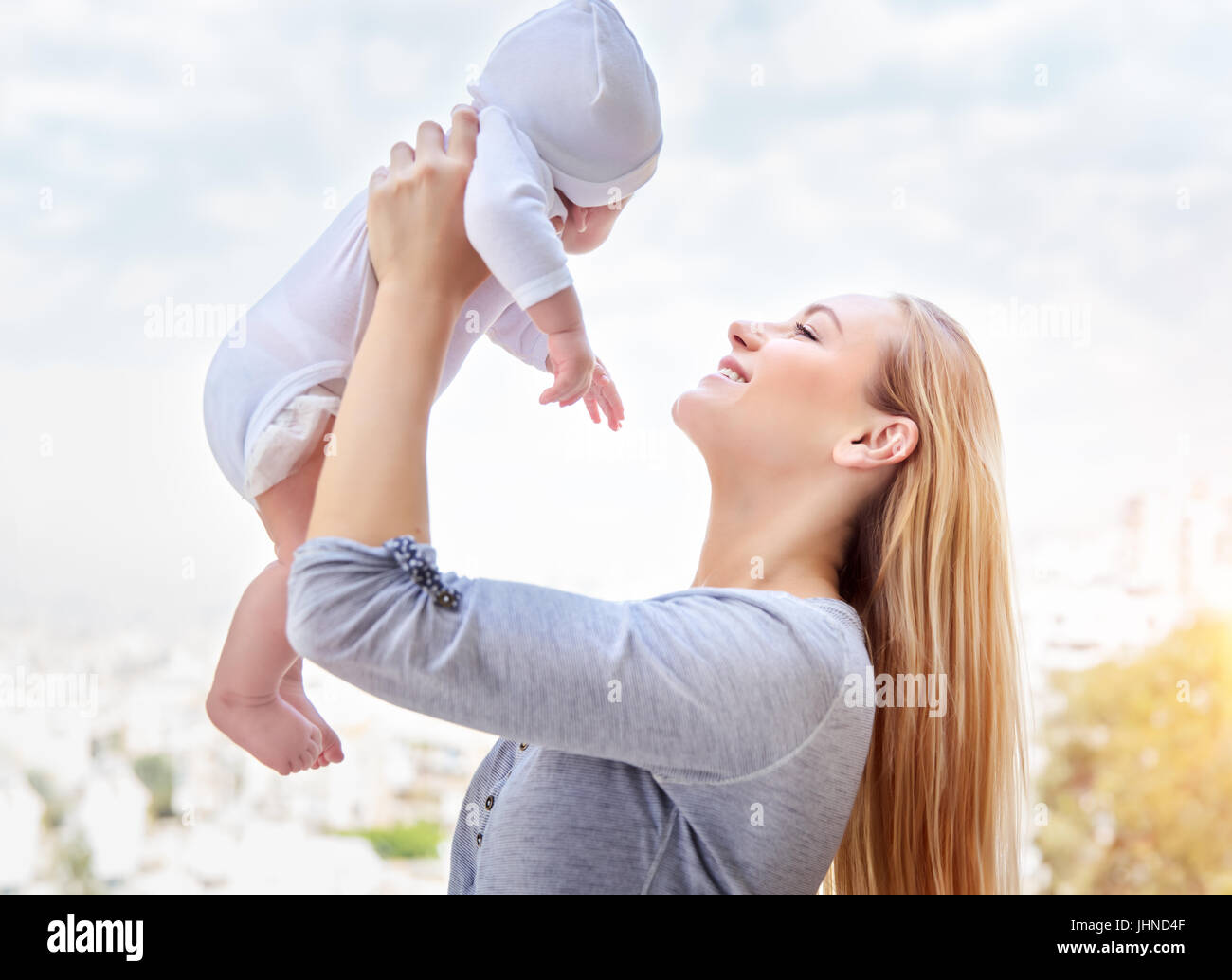 Happy mother with baby having fun outdoors, joyful young mom lifting up ...