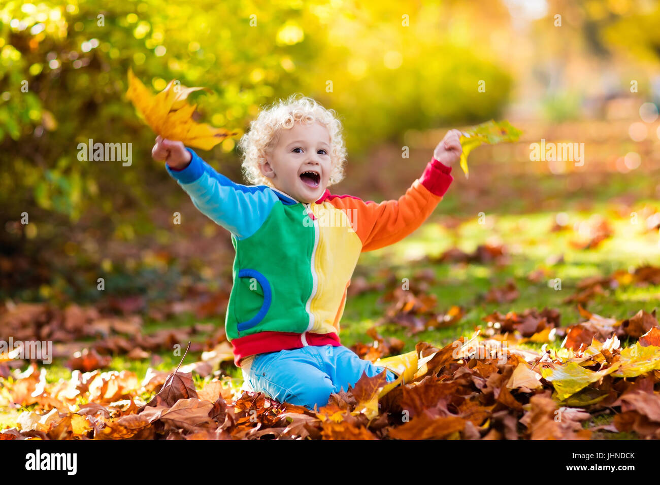 Kids play in autumn park. Children throwing yellow and red leaves ...