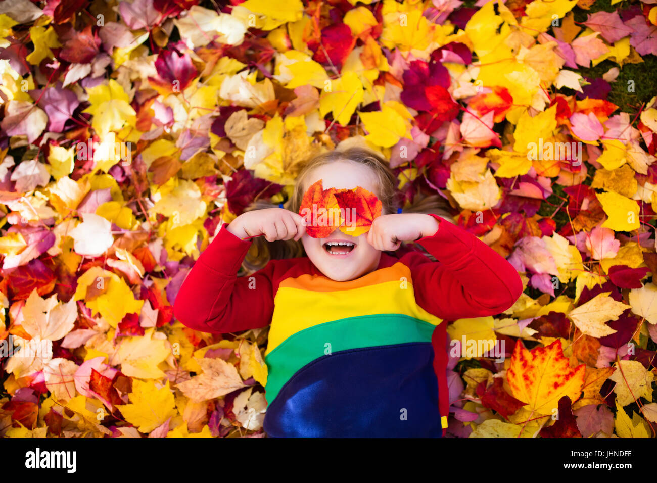 Kids play in autumn park. Children throwing yellow and red leaves ...