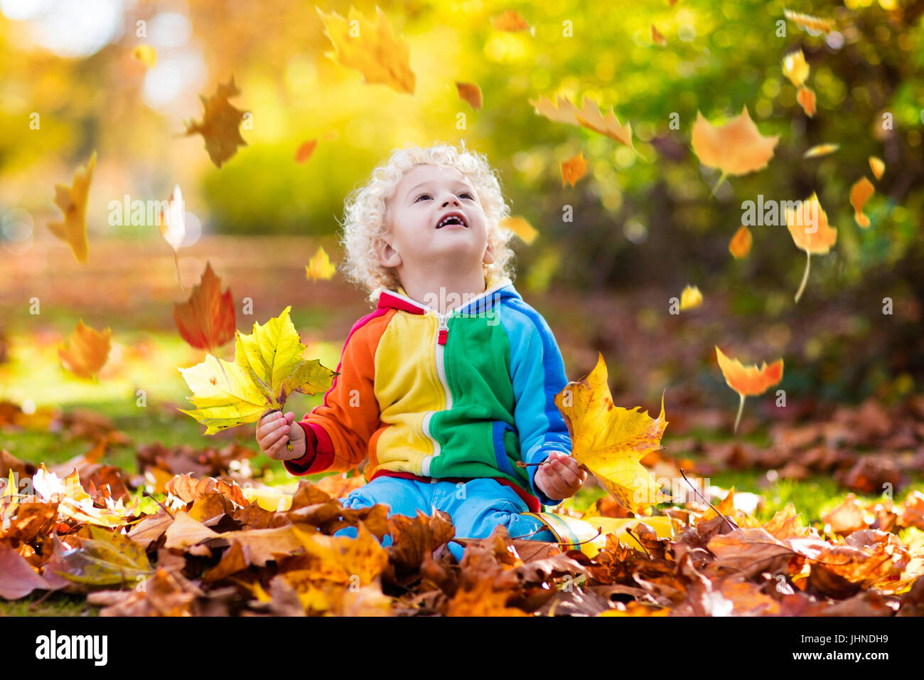 Kids play in autumn park. Children throwing yellow and red leaves ...