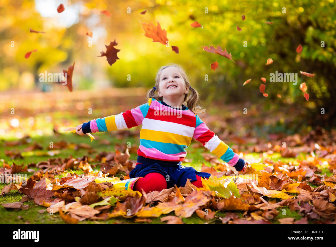 Kids play in autumn park. Children throwing yellow and red leaves ...