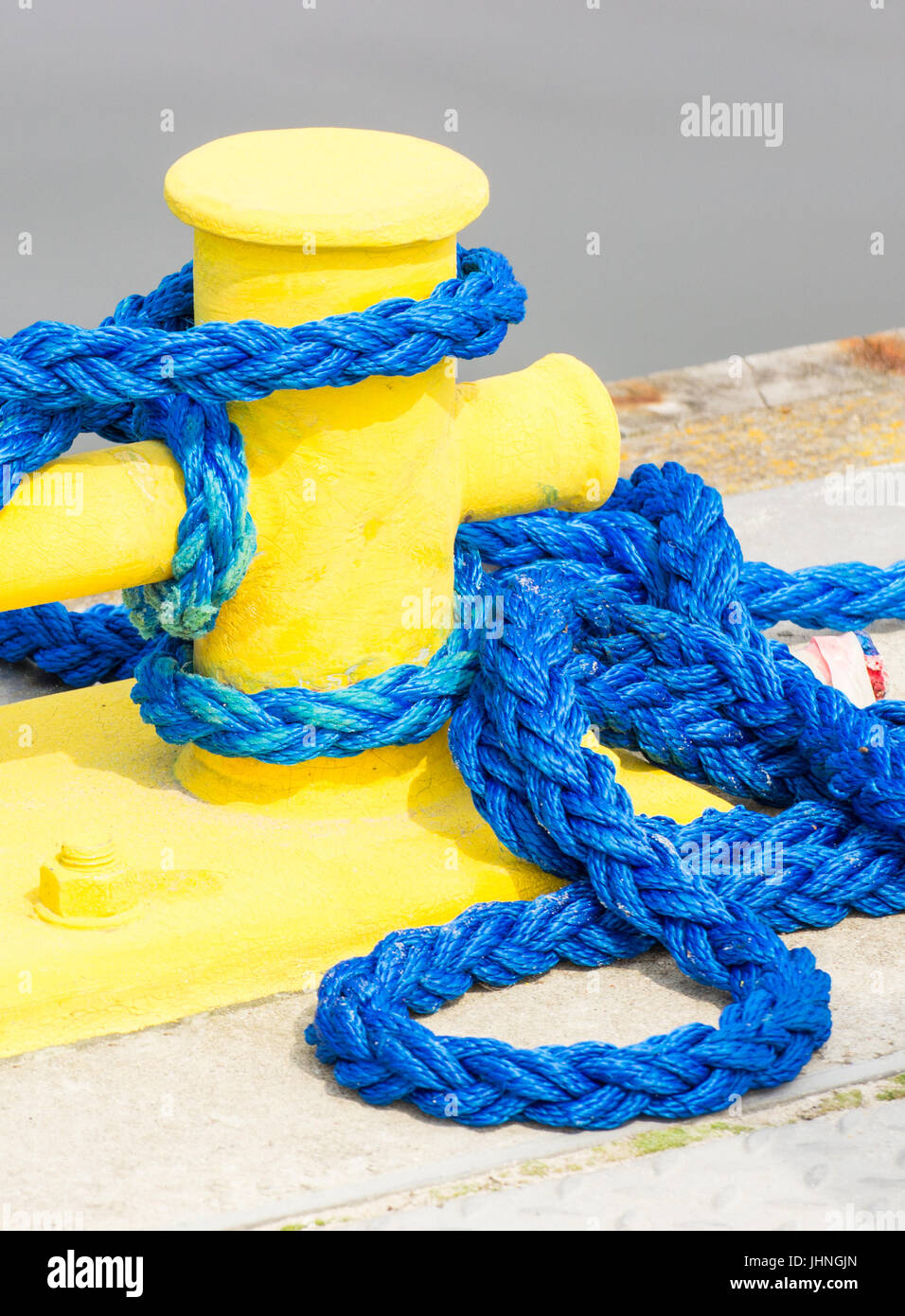 Blue rope and yellow mooring bollard in port, closeup and detail of ...