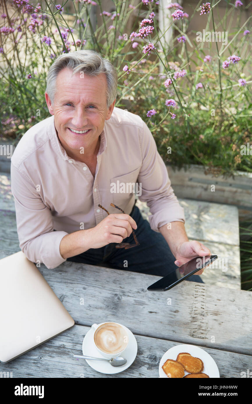 Portrait smiling senior man using digital tablet and drinking coffee at ... Portrait smiling senior man using digital tablet and drinking coffee at ...