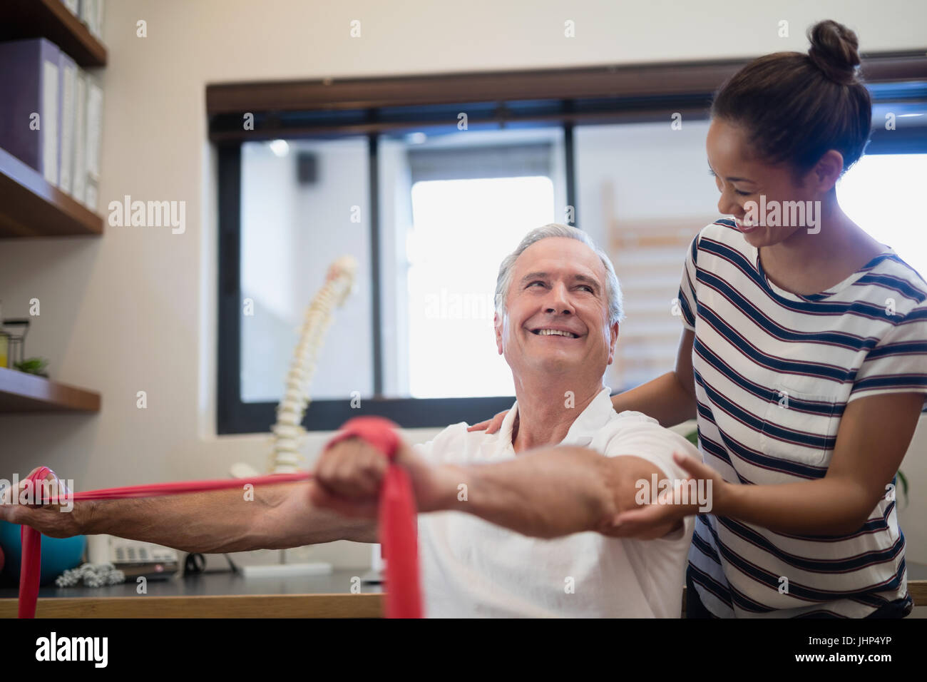 Smiling senior male patient pulling red resistance band while looking ...