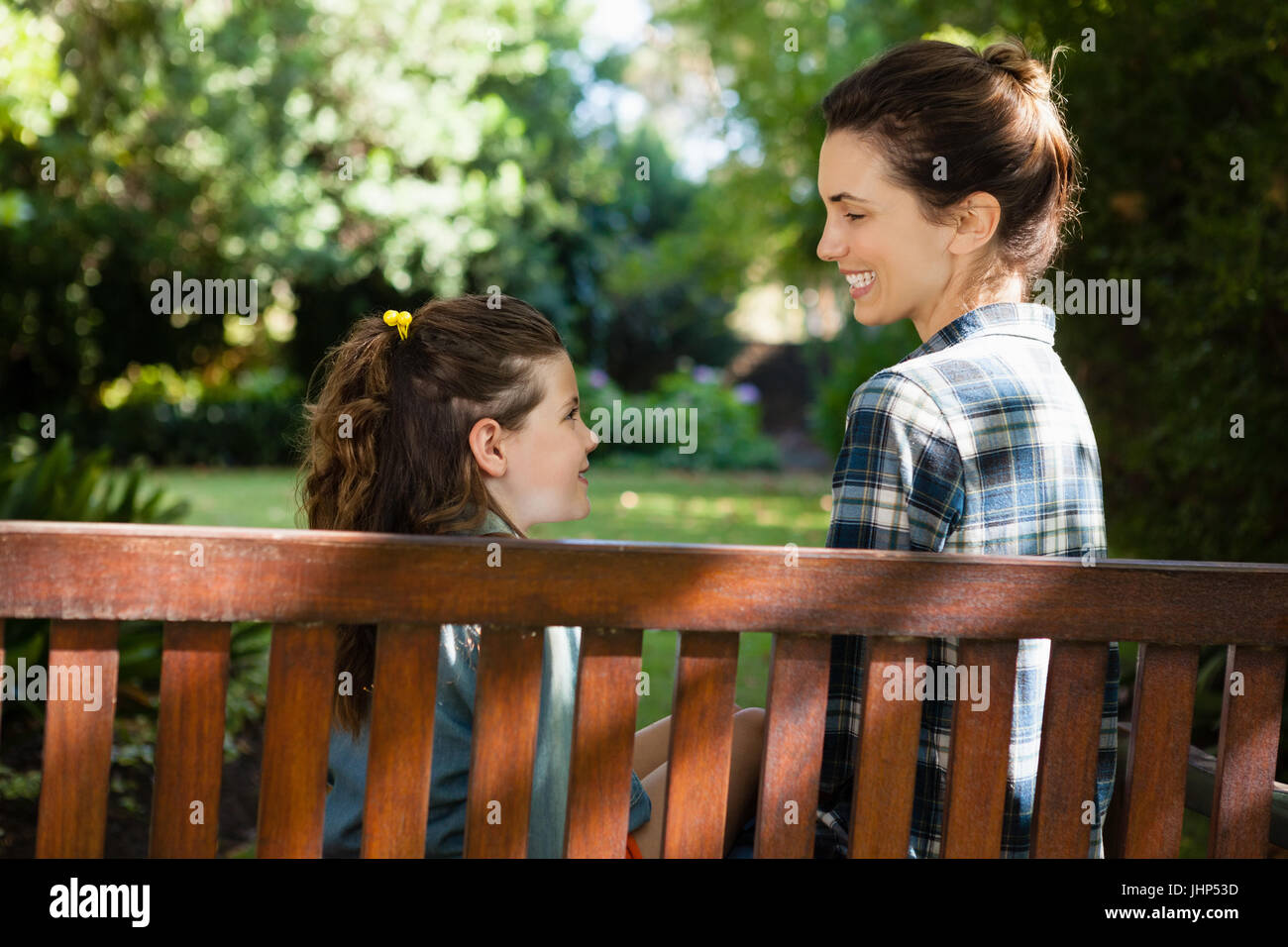 Smiling mother and daughter sitting on wooden bench in backyard Stock ...