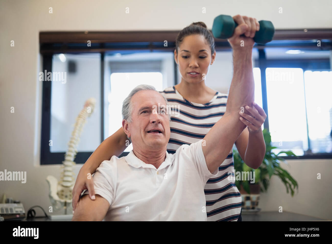 Female doctor looking at senior patient lifting dumbbell in hospital ...