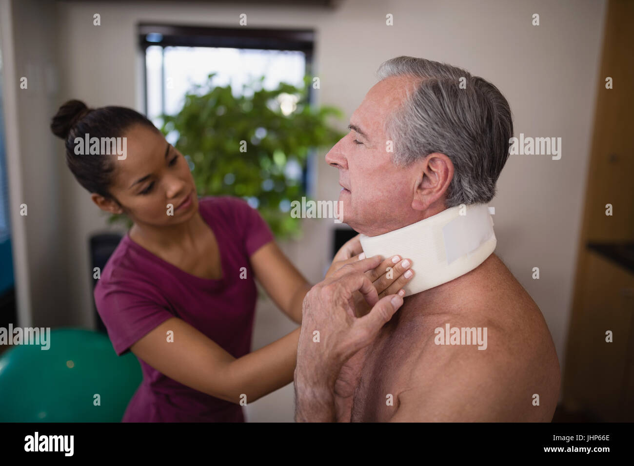 Female therapist examining neck collar on senior male patient at ...