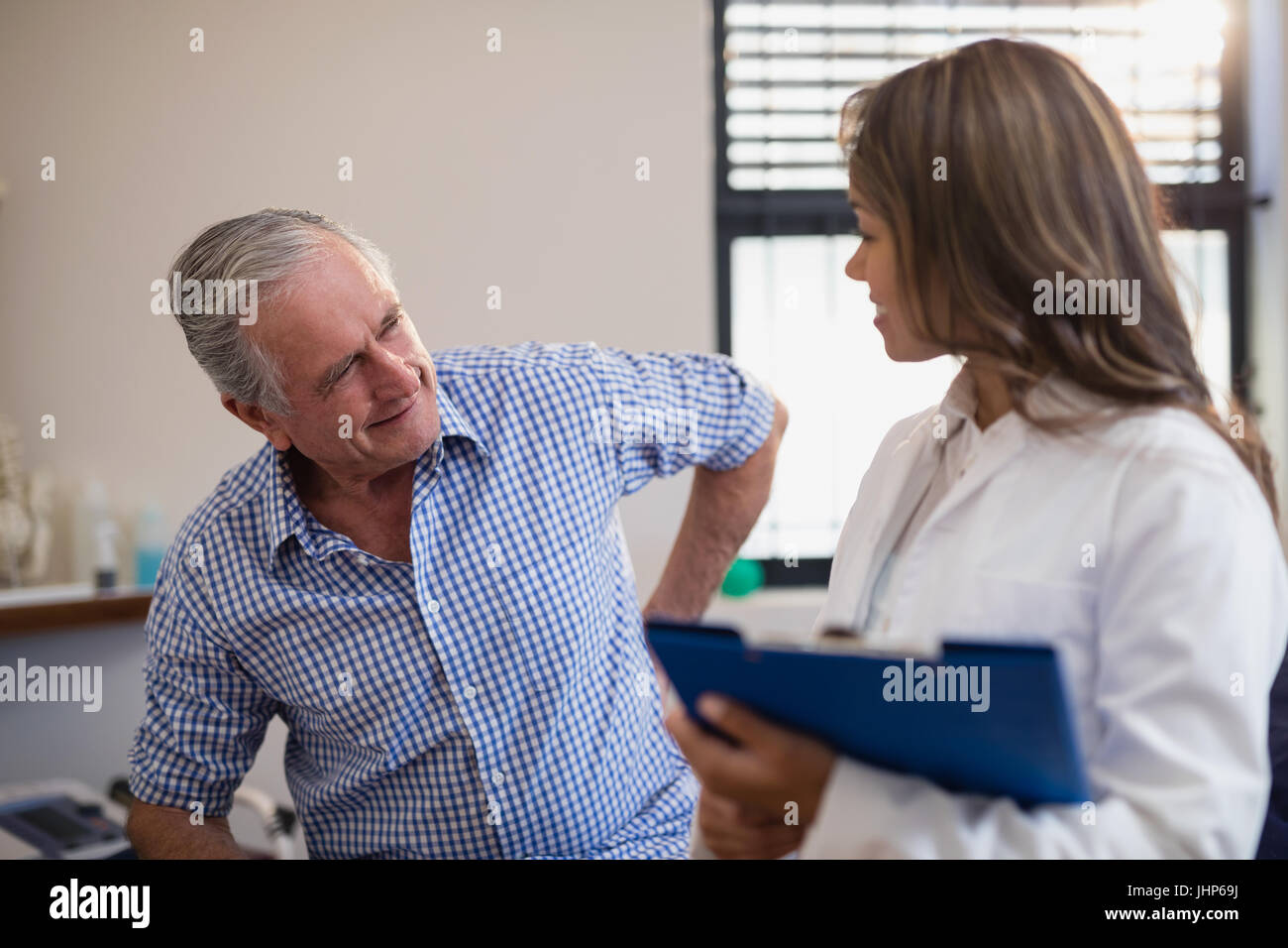 Senior male patient showing back ache to female doctor with file at ...