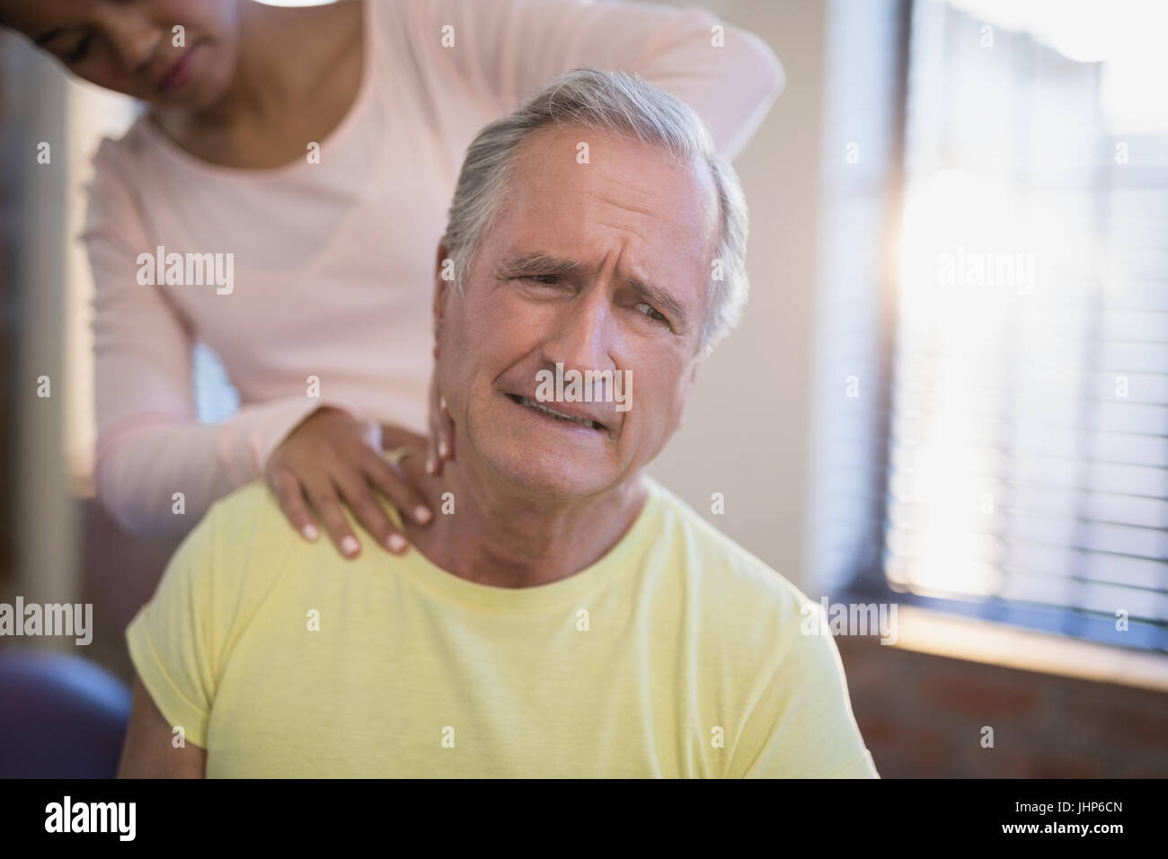 Senior male patient frowning while receiving neck massage from ...