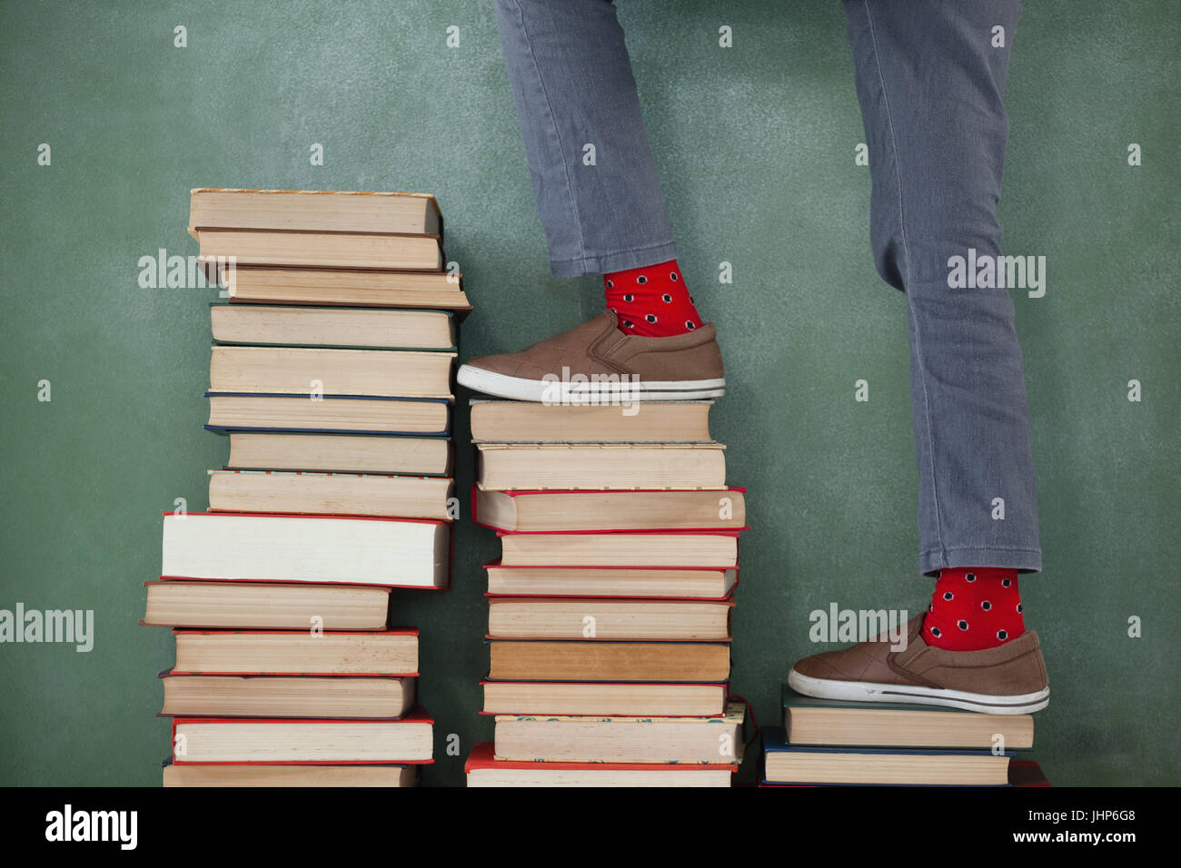 Low-section of schoolboy climbing steps of books stack against ...