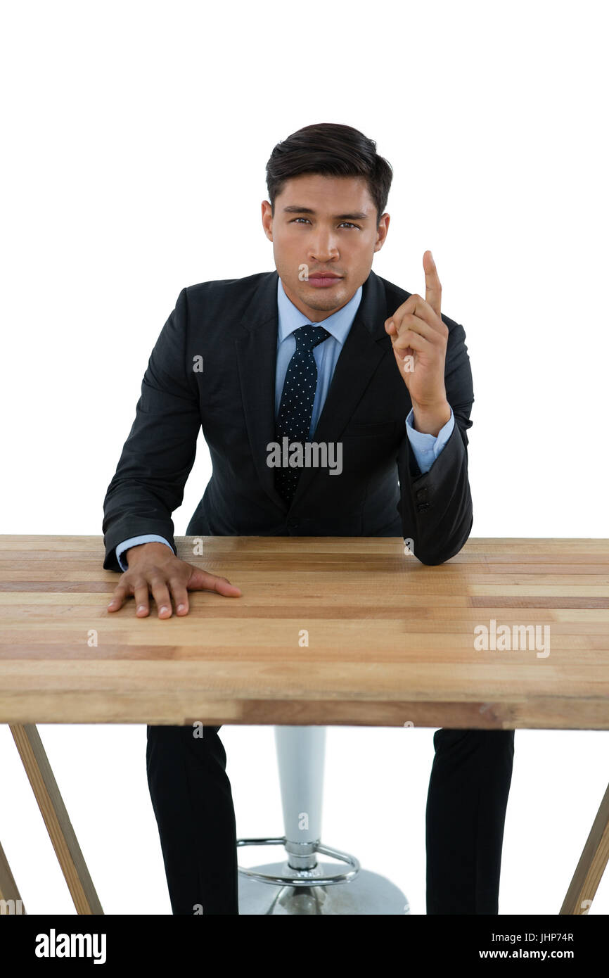 Portrait of businessman pointing upwards while sitting at table during ...