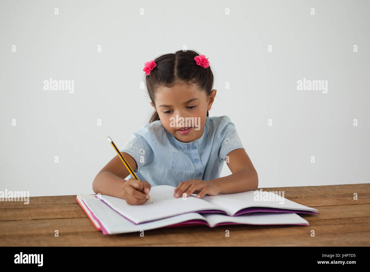 Portrait of young girl writing in her book against white background ...
