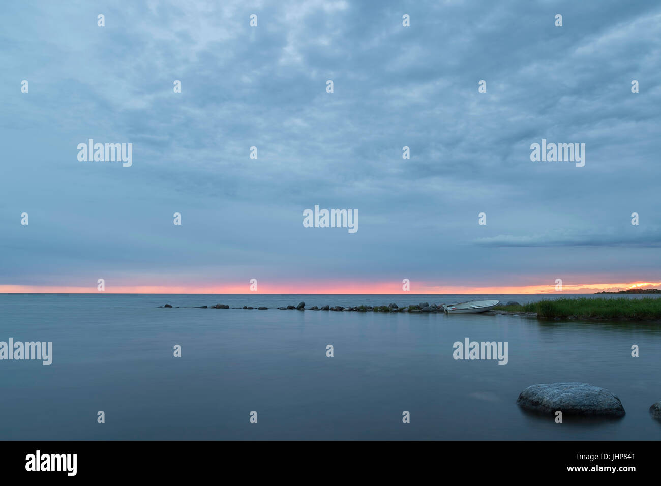 Rowboat by Ocean at Sunset with a partly cloudy sky Stock Photo - Alamy