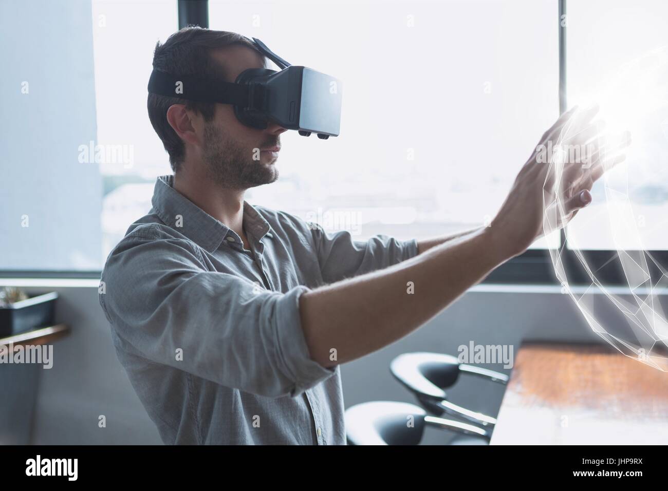 Digital composite of Man in VR headset touching a 3D sphere interface ...