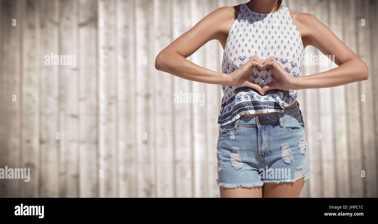 Digital composite of Millennial woman mid section making heart with ...