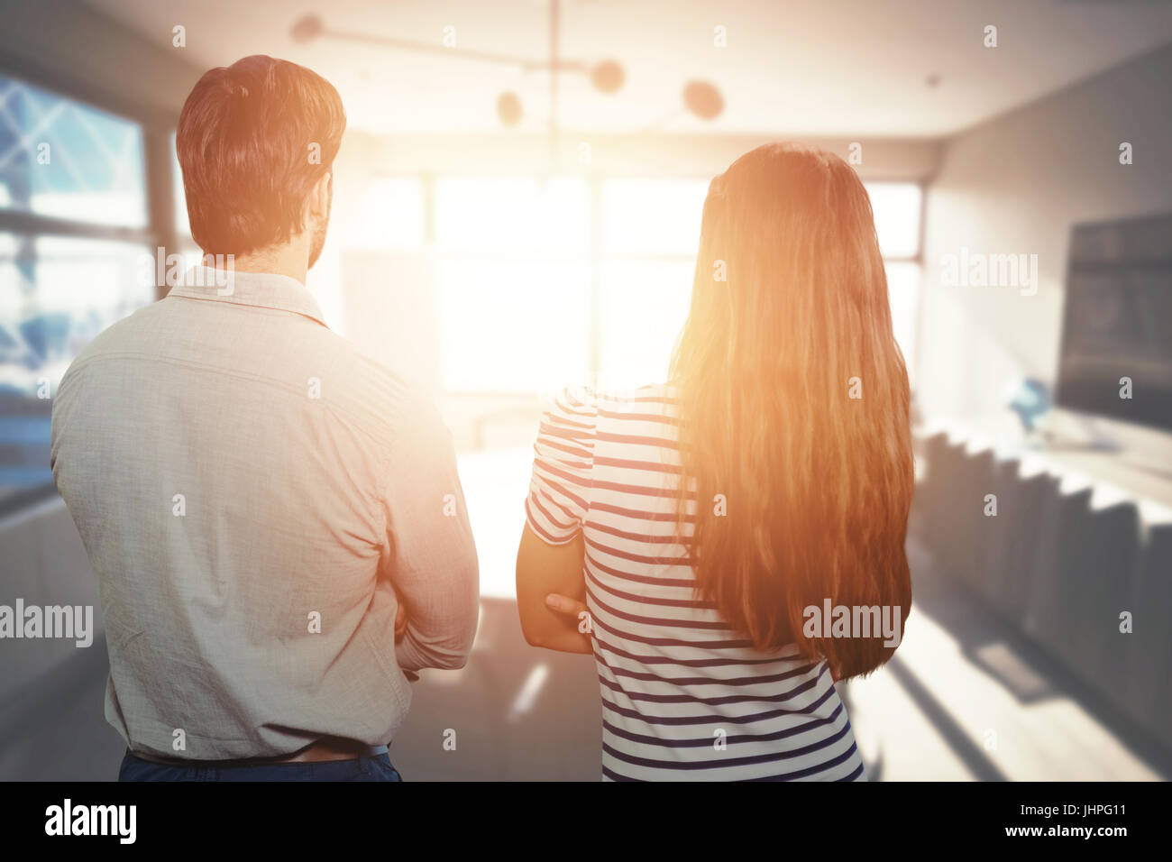 Rear view of a man and woman with crossed arms against modern empty ...