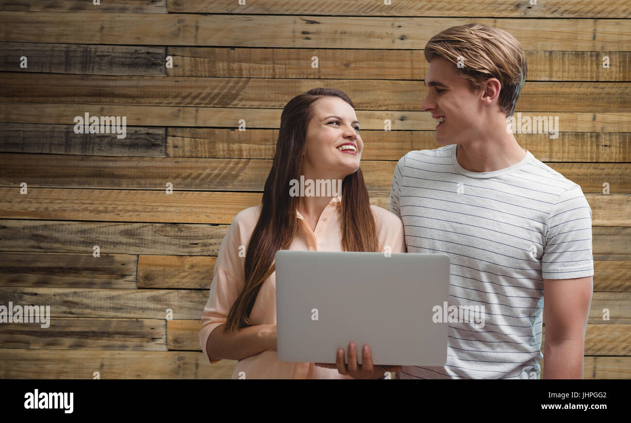 Smiling colleagues looking at each other while using laptop against ...