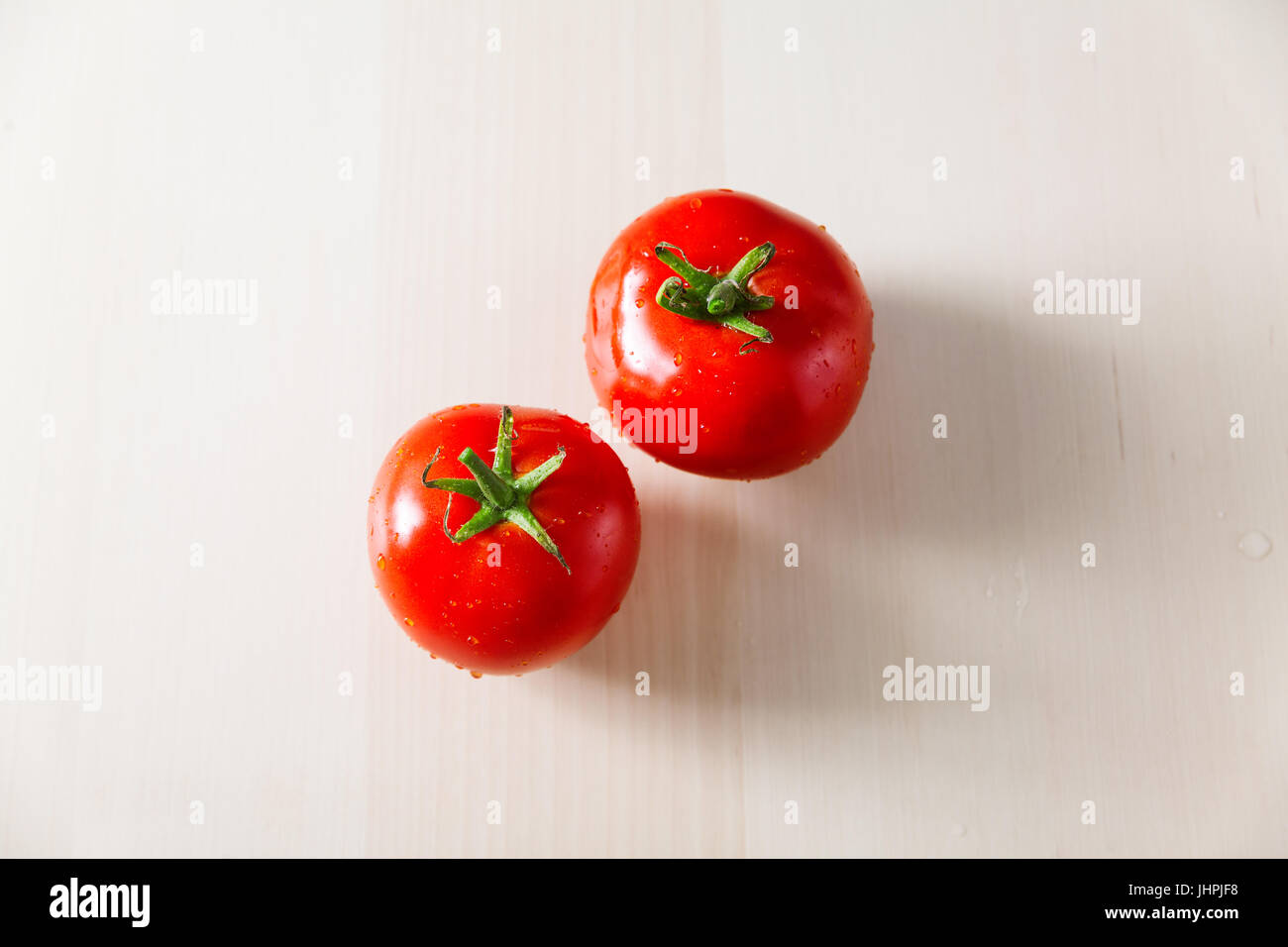 Two red ripe tomatoes on a kitchen table of light wood Stock Photo - Alamy