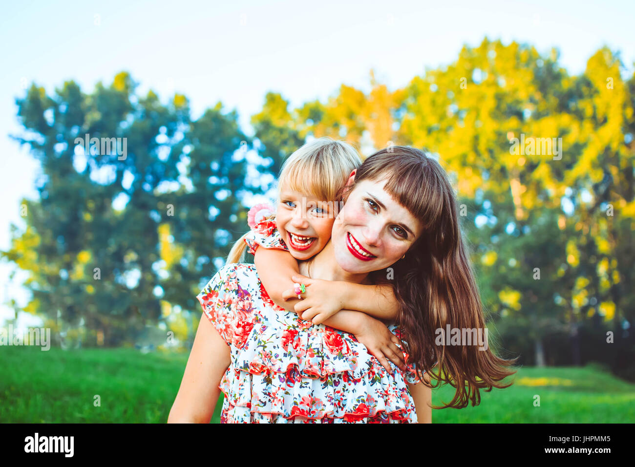 Cute young daughter on a piggy back ride with her mother. Looking at ...