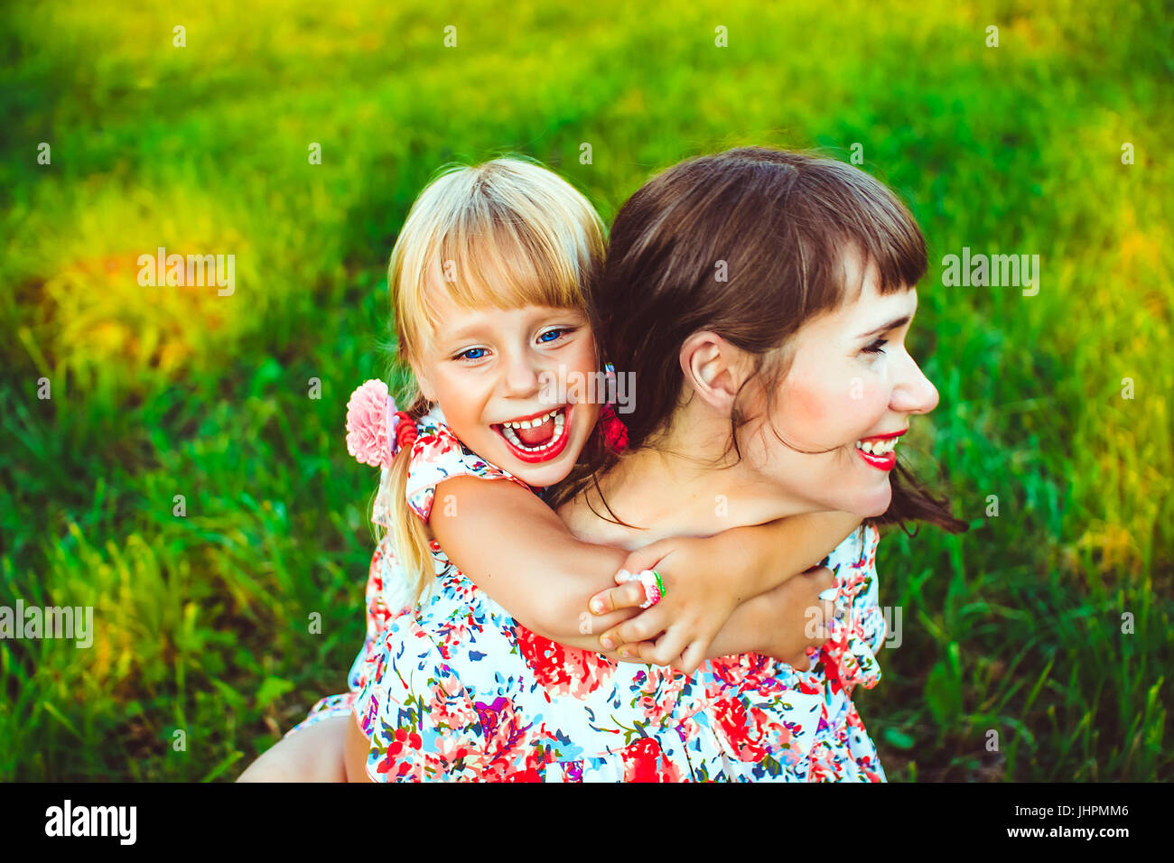 Cute young daughter on a piggy back ride with her mother. Looking at ...