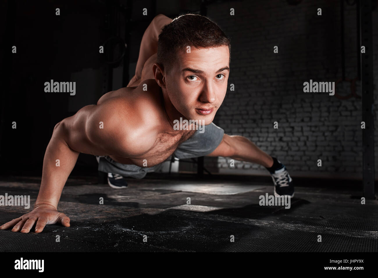 Portrait of a young sportsman doing push ups exercise with one hand ...