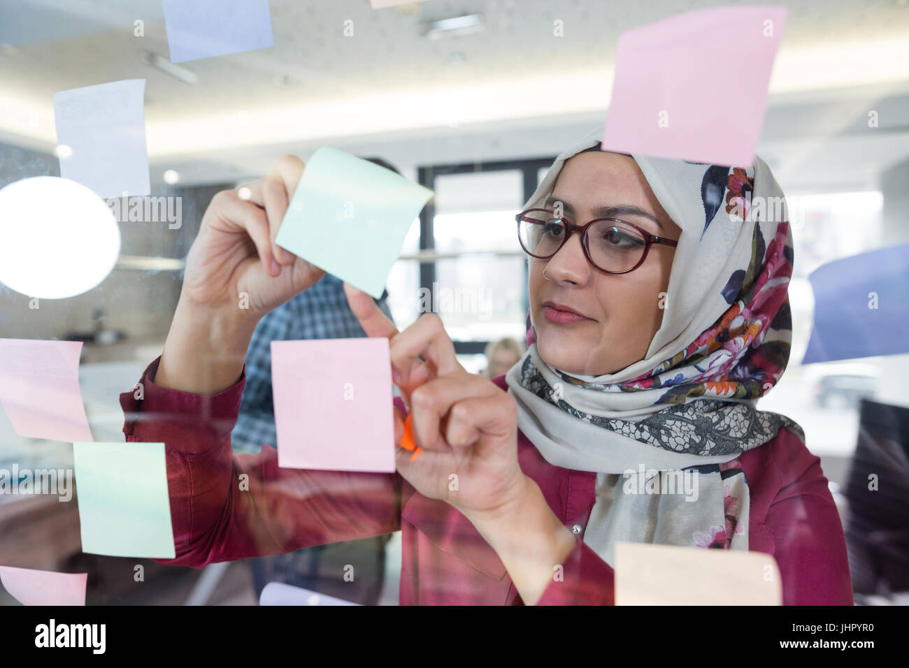 Beautiful Arab woman wearing hijab putting sticky notes on glass in ...