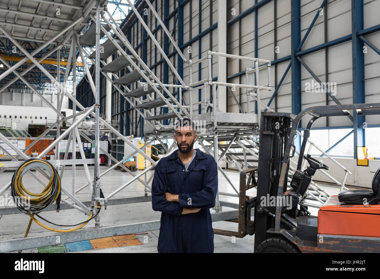 Portrait of aircraft maintenance engineer standing with arms crossed at ...