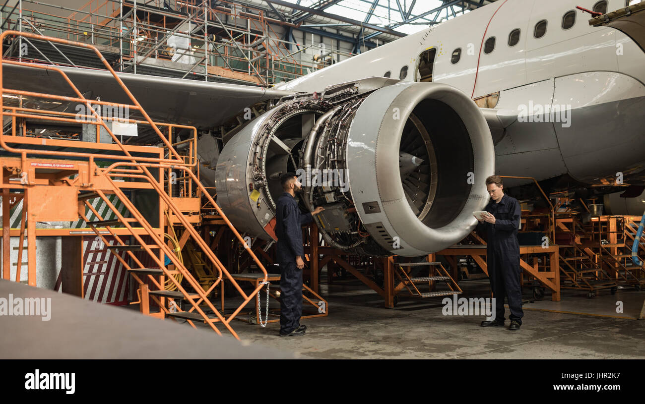 Aircraft maintenance engineers examining turbine engine of aircraft at ...