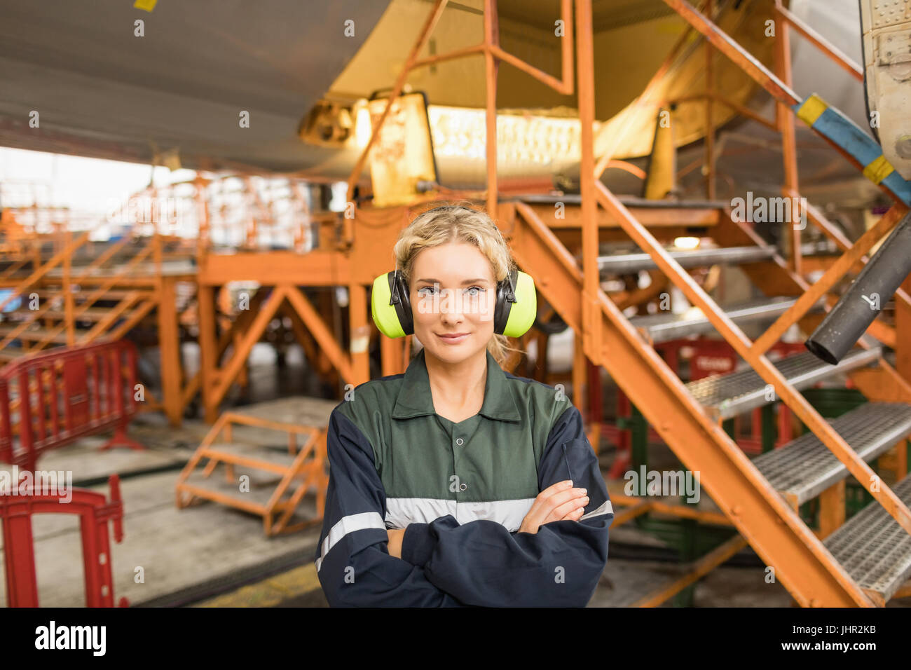 Portrait of female aircraft maintenance engineer standing with arms ...