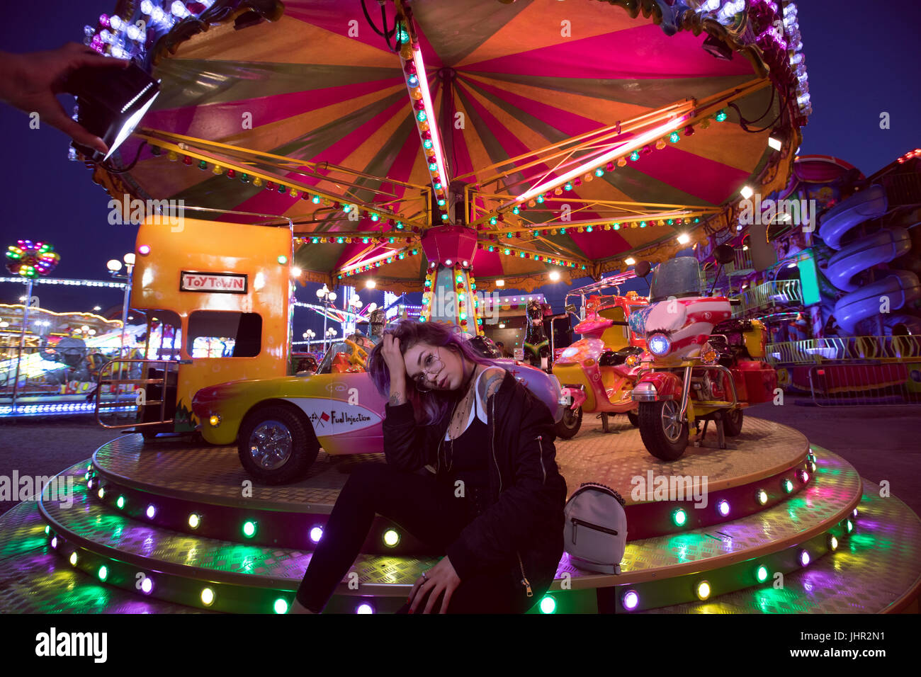 Portrait of beautiful woman sitting near carousel in amusement park at ...