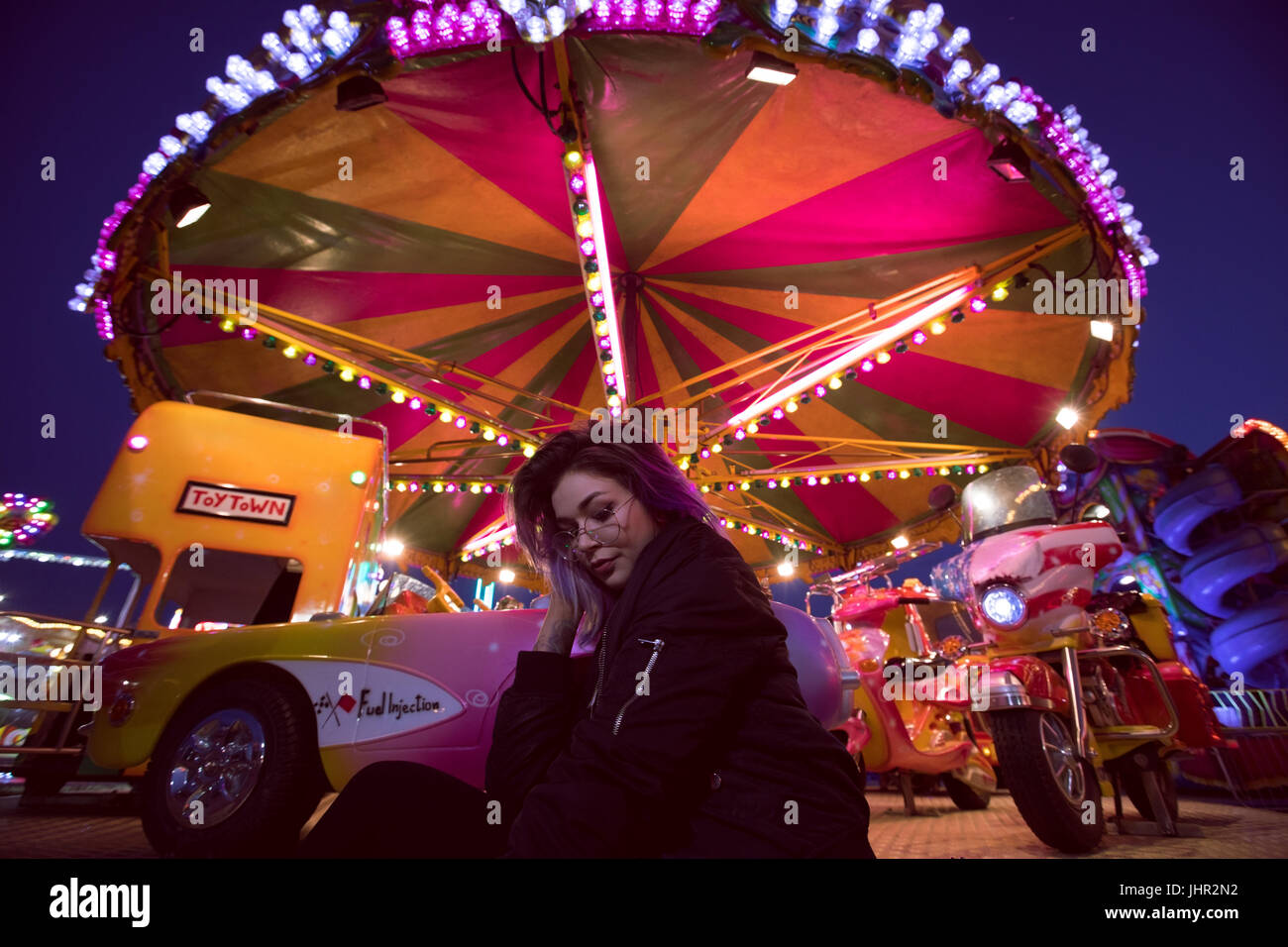 Portrait of beautiful woman sitting near carousel in amusement park at ...