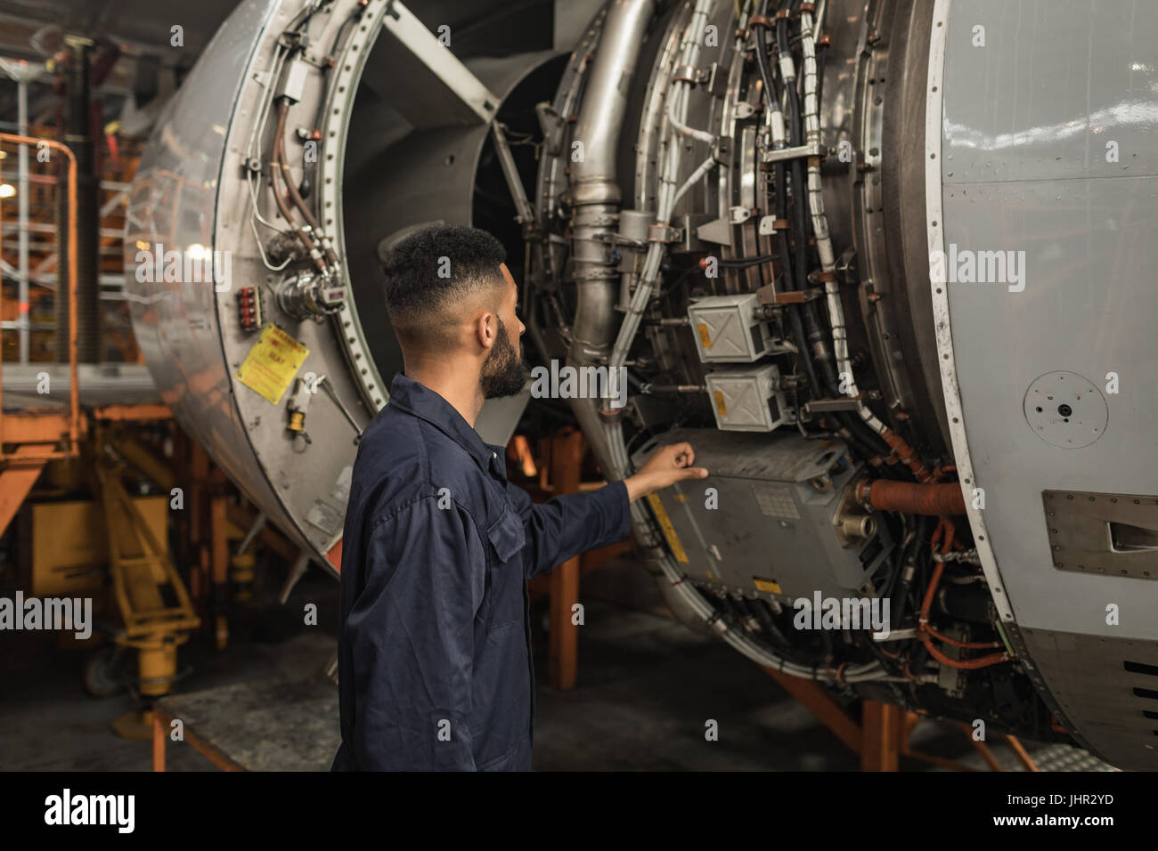 Male aircraft maintenance engineer examining turbine engine of aircraft at airlines maintenance ...