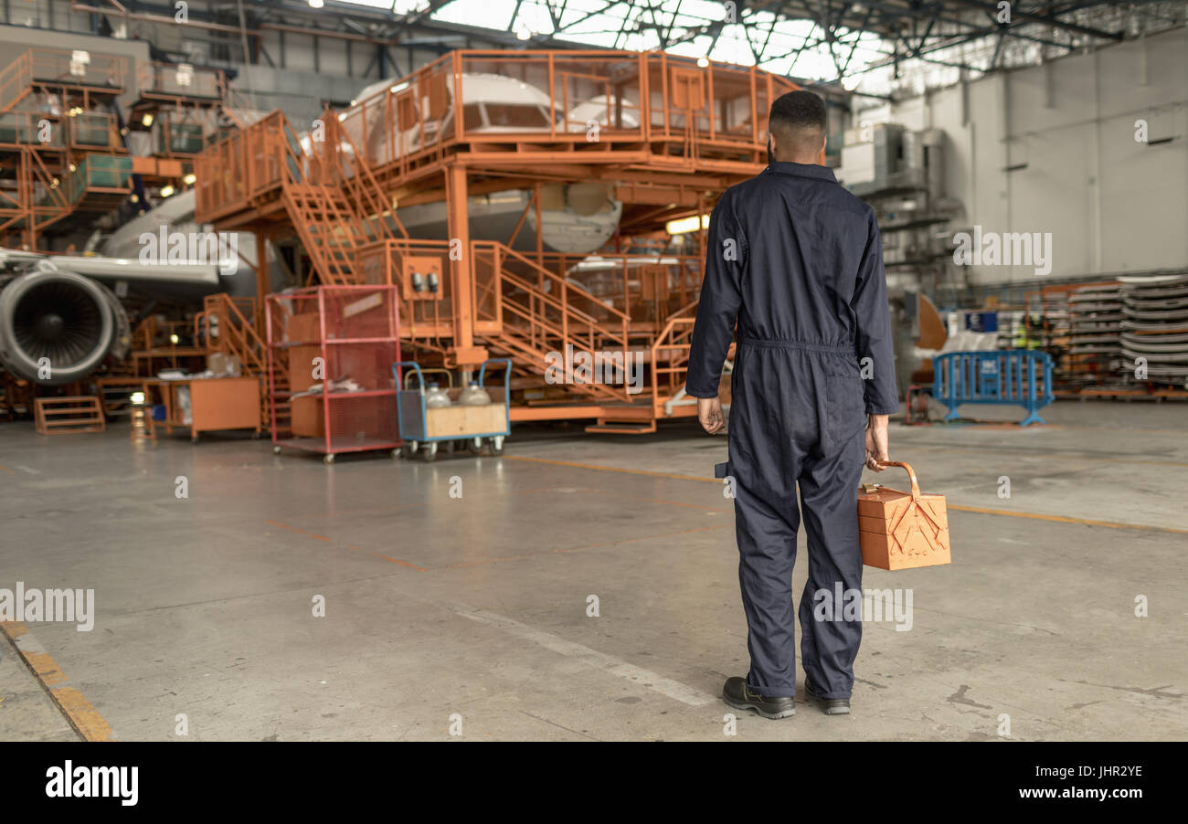Rear view of male aircraft maintenance engineer holding tool kit at ...