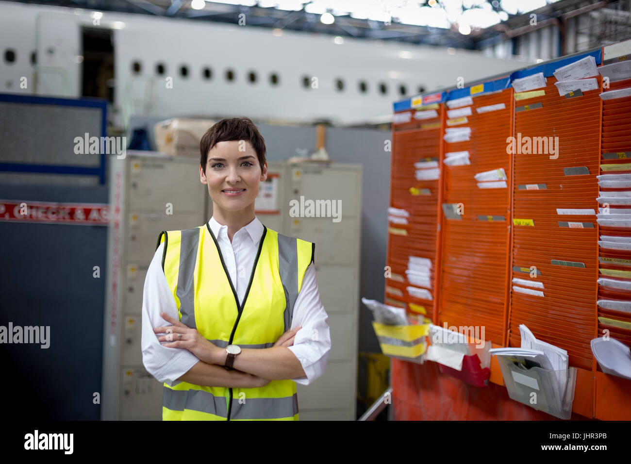 Portrait of female aircraft maintenance engineer standing with arms ...