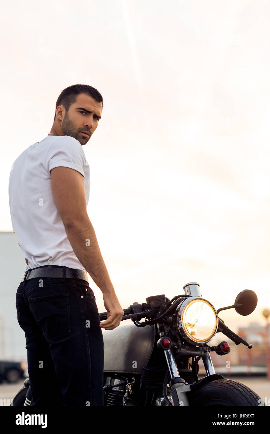 Sporty biker handsome rider man in white blank t-shirt walk to classic ...