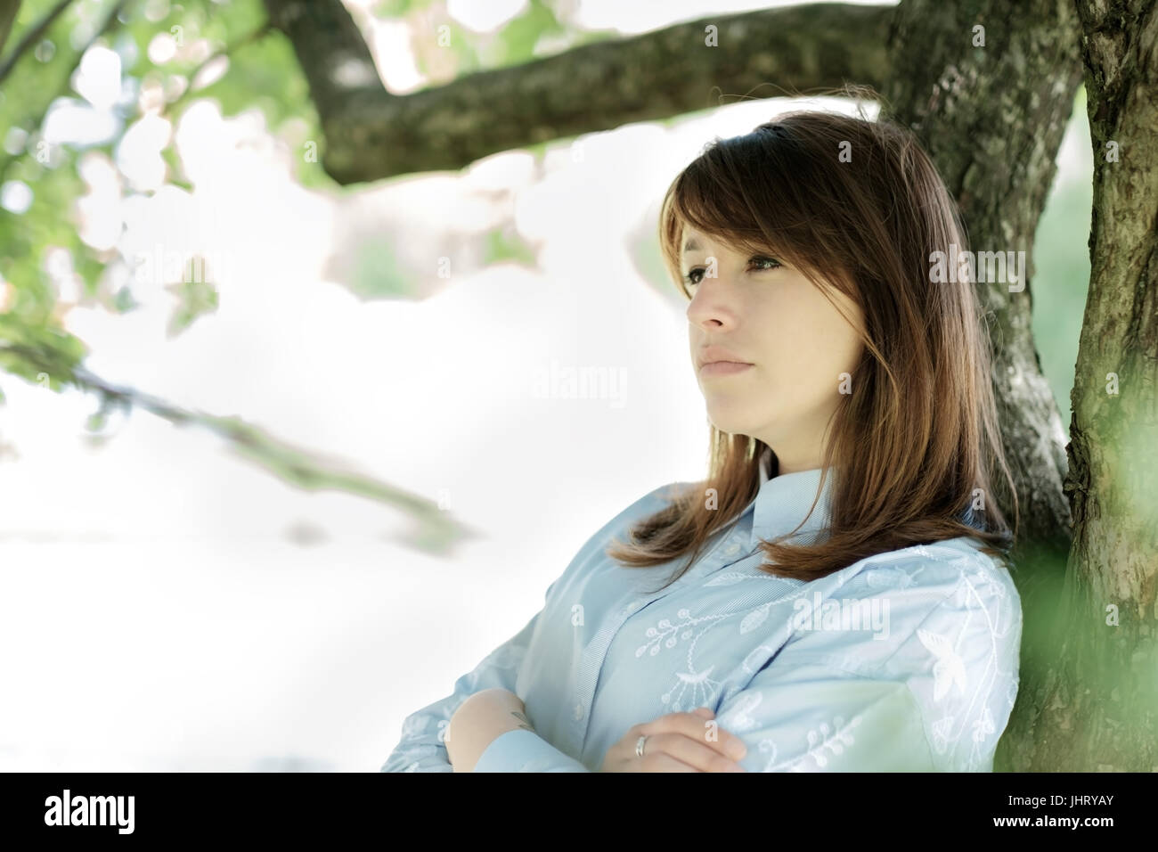 A woman leaning against a big tree alone in the park Stock Photo - Alamy