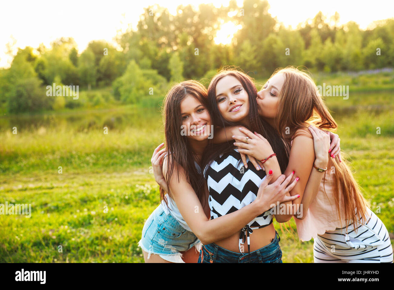 three women hugging each other outdoors and laughing on sunset ...