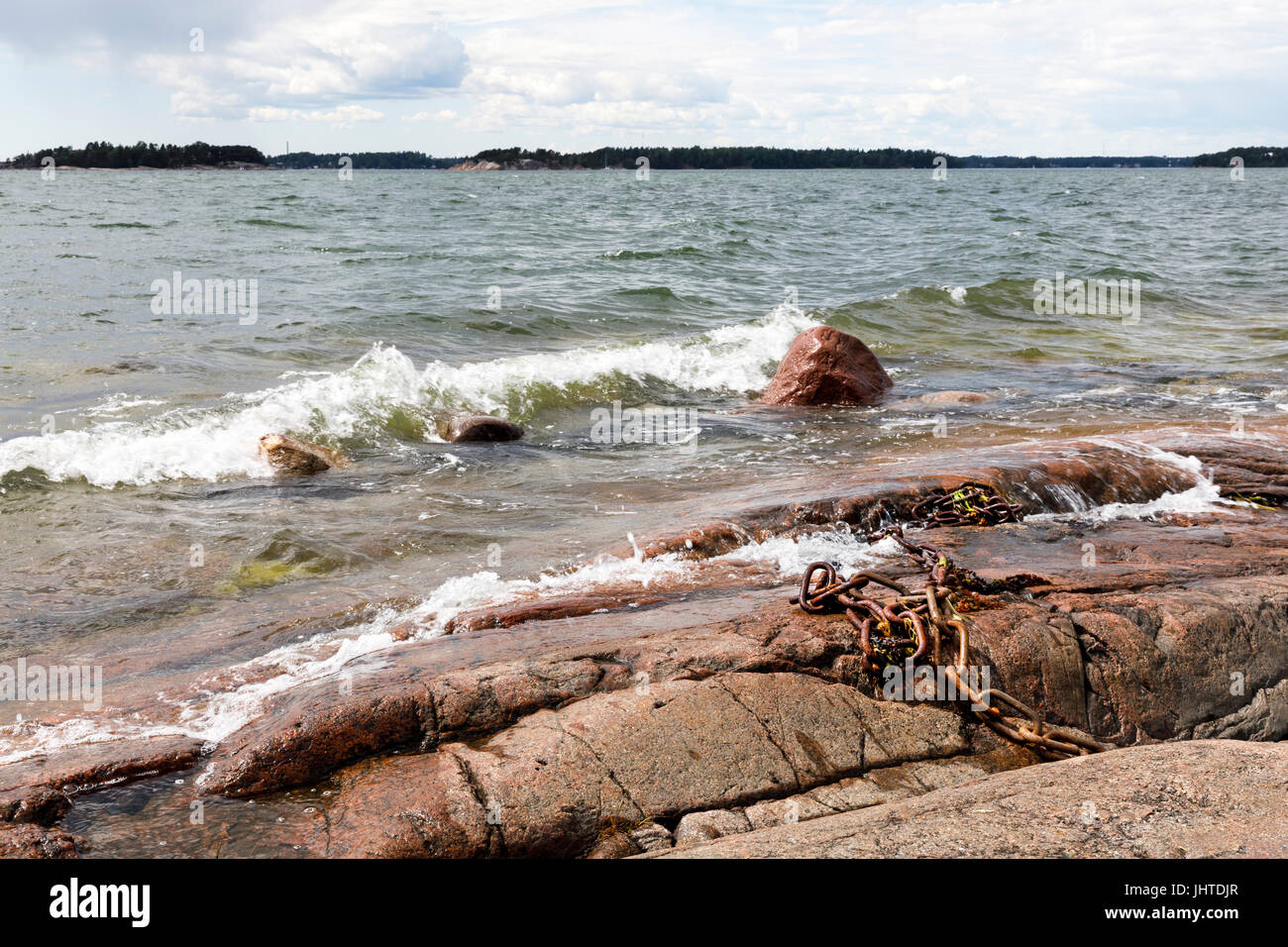 White foamy water waves hit into rocky seashore. Old rusty iron chain ...